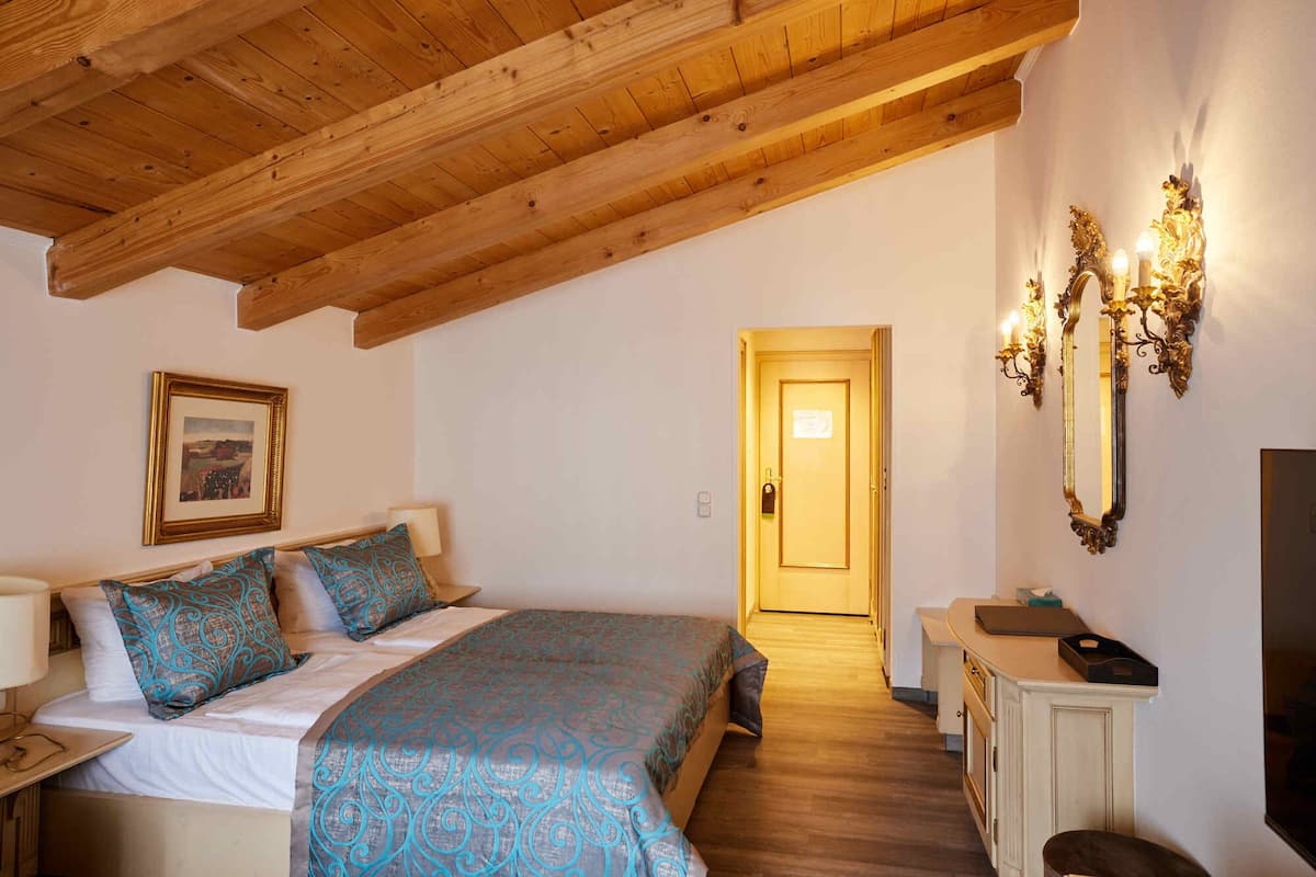 Quarto com teto de madeira, cama com roupa de cama estampada, mesa de cabeceira, cómoda e espelho com arandelas.