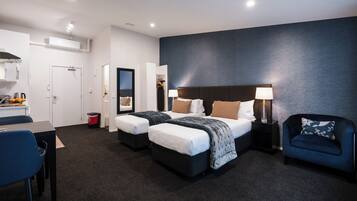 Quarto de hotel com duas camas, uma escrivaninha, uma cadeira, um guarda-roupa e uma mesa de cabeceira com abajur.