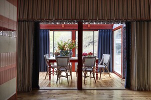Quarto com piso de madeira, parede vermelha e uma grande porta de vidro deslizante que dá para área externa com mesa e cadeiras.