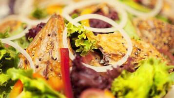 Um close-up de uma salada com diversos vegetais e um pedaço de peixe grelhado.