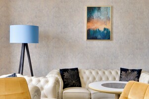 Um quarto com um sofá estofado, uma mesa redonda, um abajur e um quadro abstrato na parede.