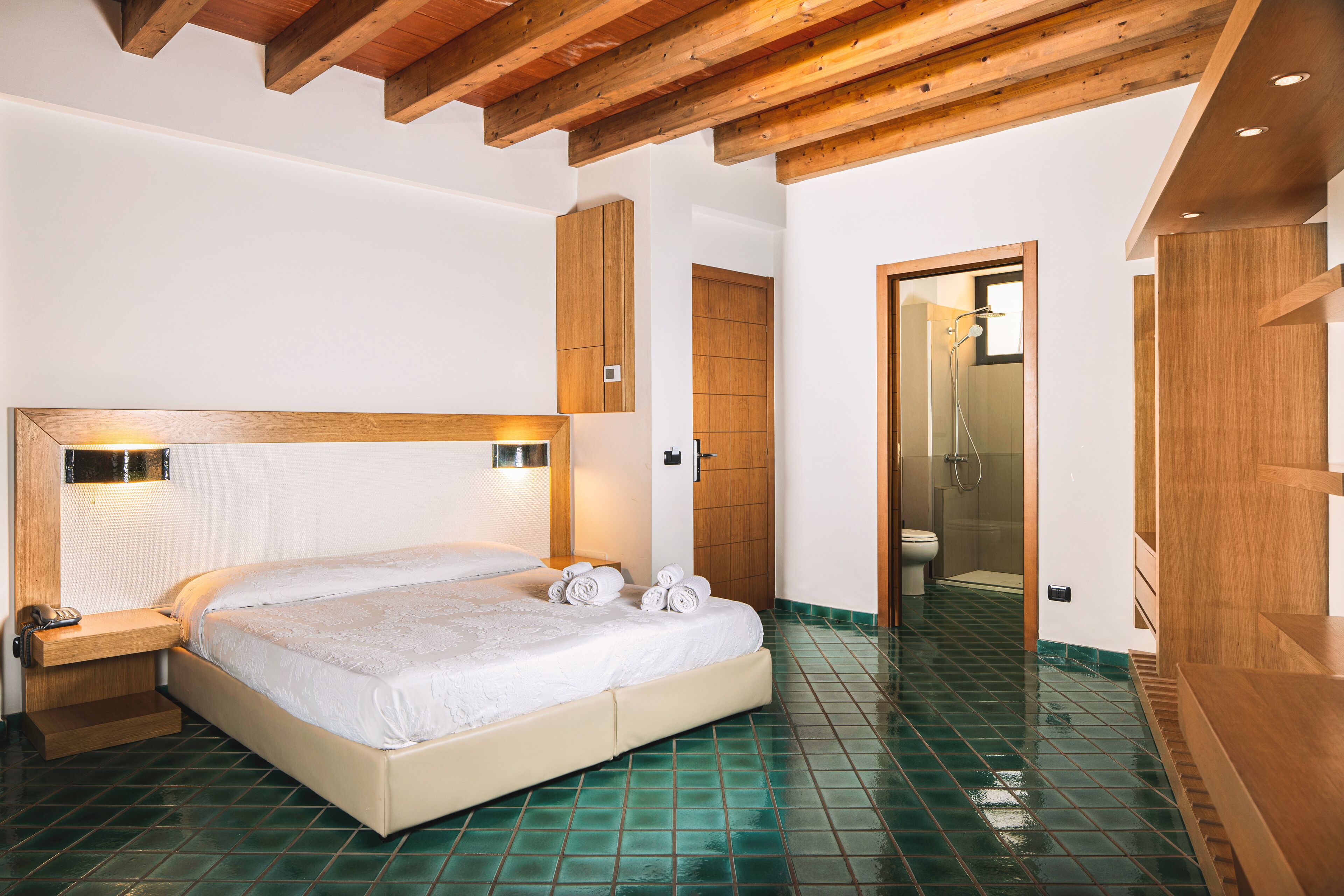 Quarto com uma cama grande, cabeceira de madeira, mesas de cabeceira e um banheiro visível por uma porta aberta.