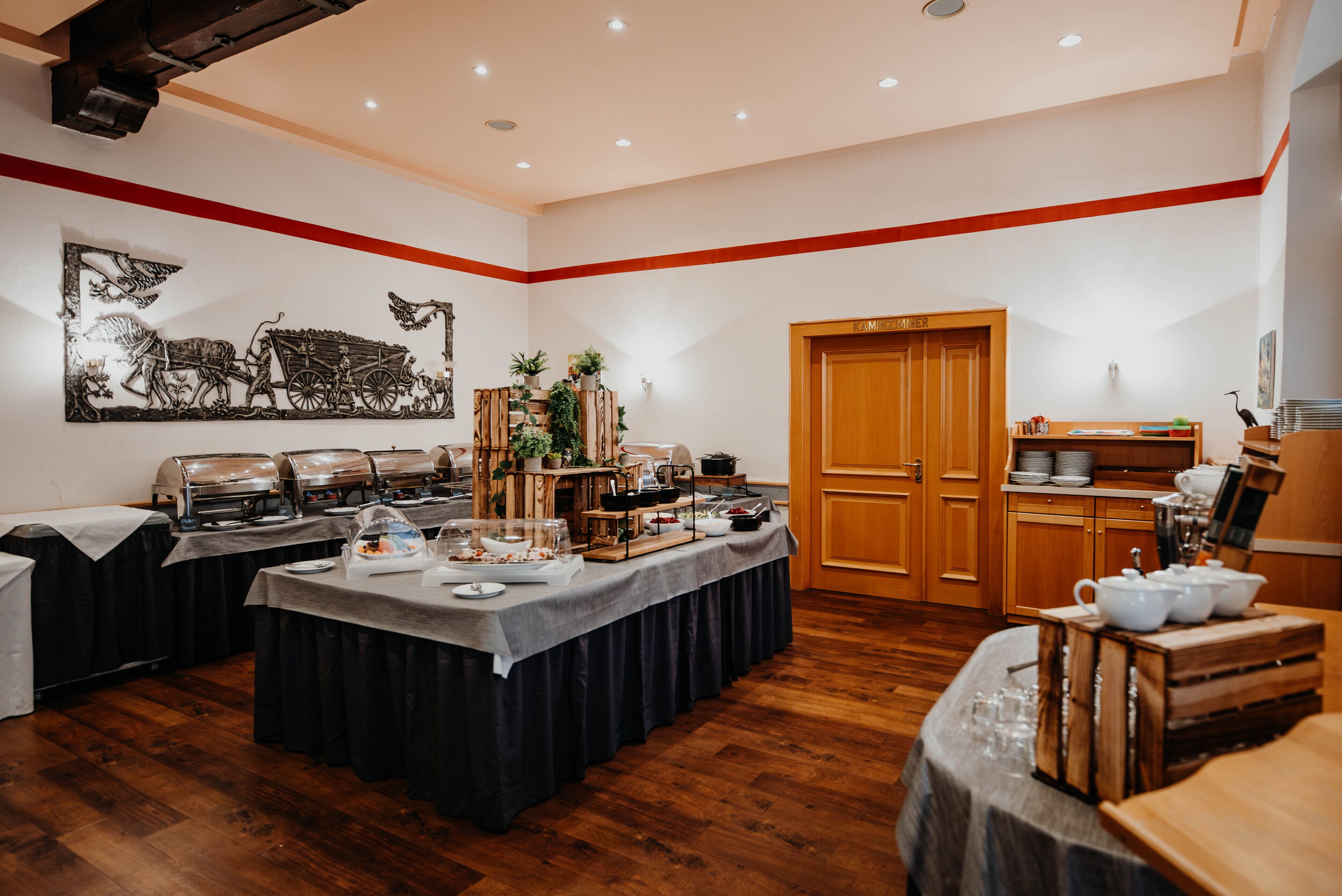 Buffet montado com diversas estações de serviço, uma porta de madeira e uma área de cozinha com utensílios e louças.