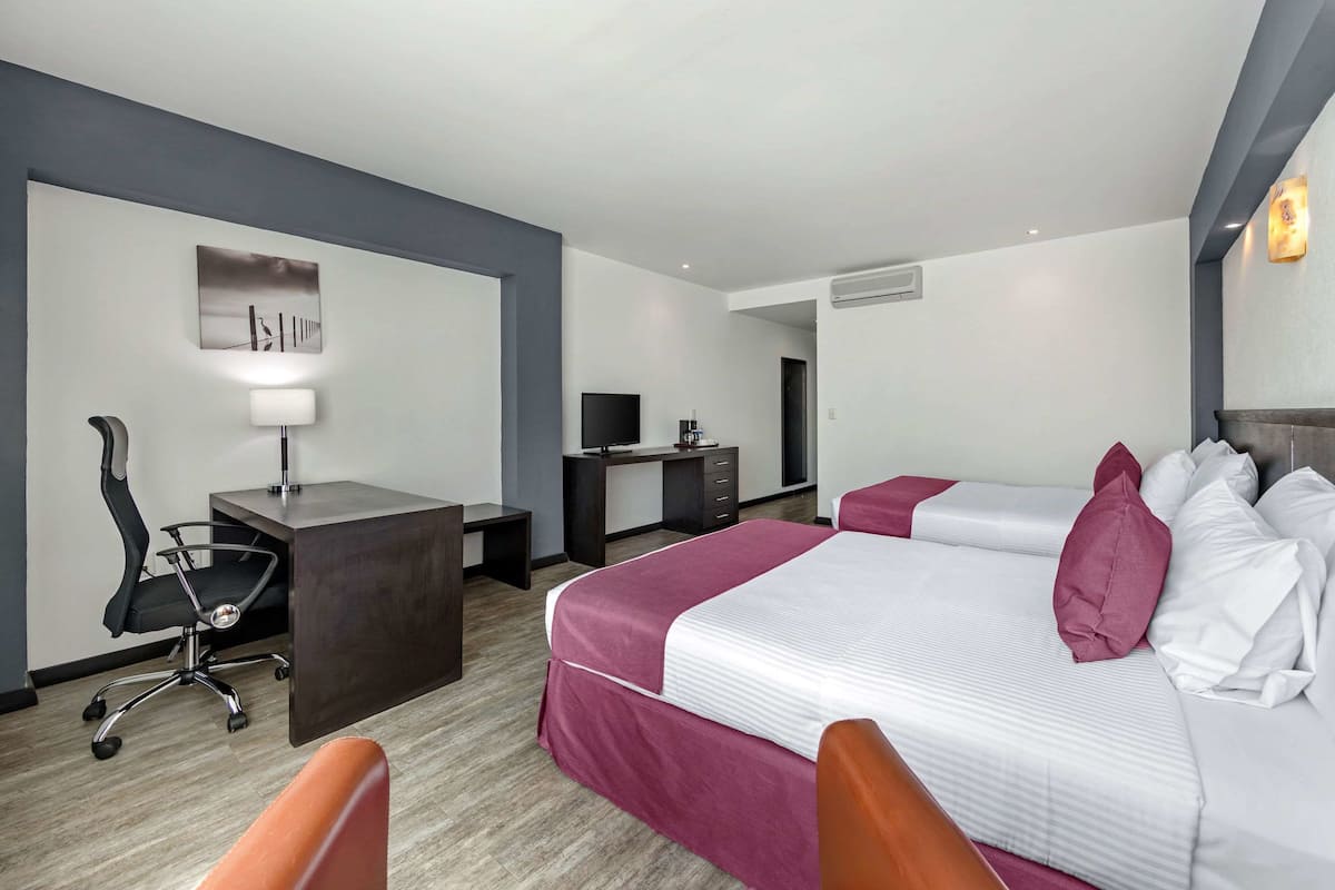 Quarto de hotel com cama, escrivaninha, cadeira e televisão.