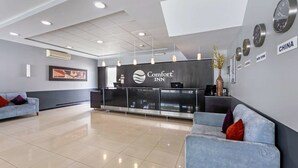 Um hall de hotel moderno com balcão de recepção, áreas de estar e relógios mostrando diferentes fusos horários.