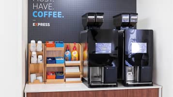 Um espaço com estação de café, duas máquinas de café, um dispensador de café e um aviso que diz "MUST. HAVE. COFFEE. EXPRESS.".