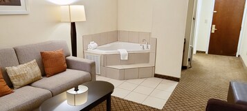 Quarto de hotel com sofá, mesa, luminária e banheira de canto.