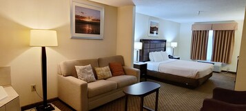 Quarto de hotel com cama, sofá, mesinha, criado-mudo, abajur e um quadro na parede.