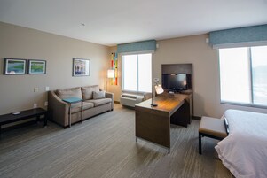 Quarto de hotel com sofá, escrivaninha, televisão e cama.