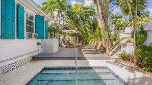Uma piscina com borda azulejada, rodeada por um espaço de pátio com cadeiras e um guarda-sol.