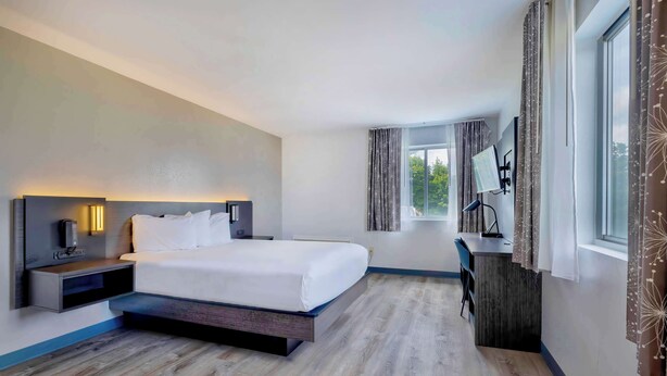 Quarto de hotel moderno com cama, mesa de cabeceira, abajur e escrivaninha com cadeira.