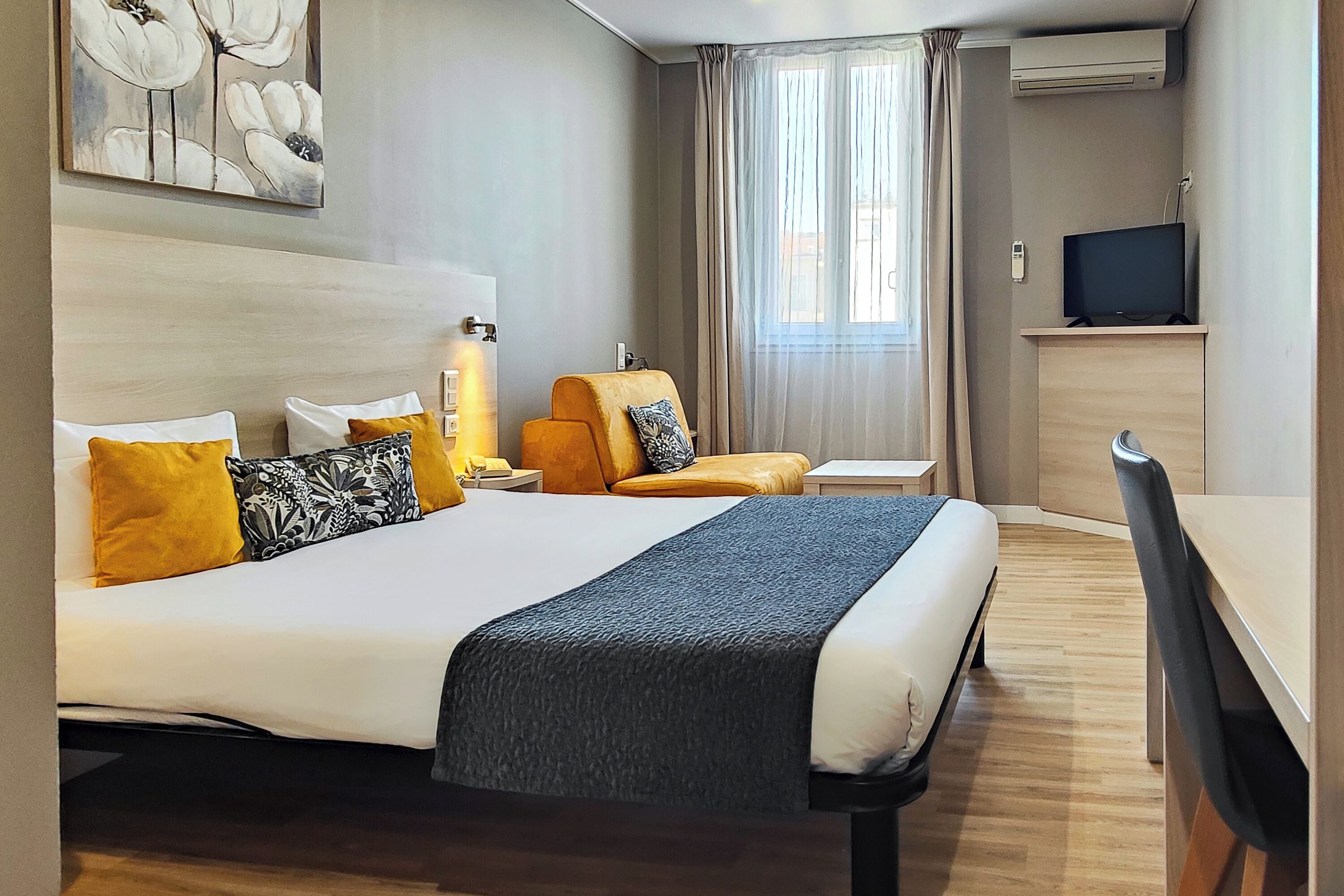 Quarto de hotel com uma cama grande, uma escrivaninha, uma cadeira, uma televisão e uma janela com cortinas.