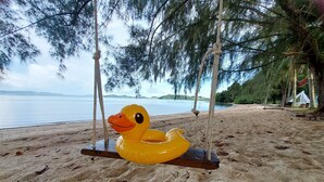 Uma praia com um balanço e um assento em formato de pato amarelo.