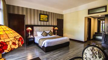 Quarto de hotel com uma cama grande, duas luminárias de cabeceira, uma mesinha de cabeceira, um espelho e um quadro na parede.