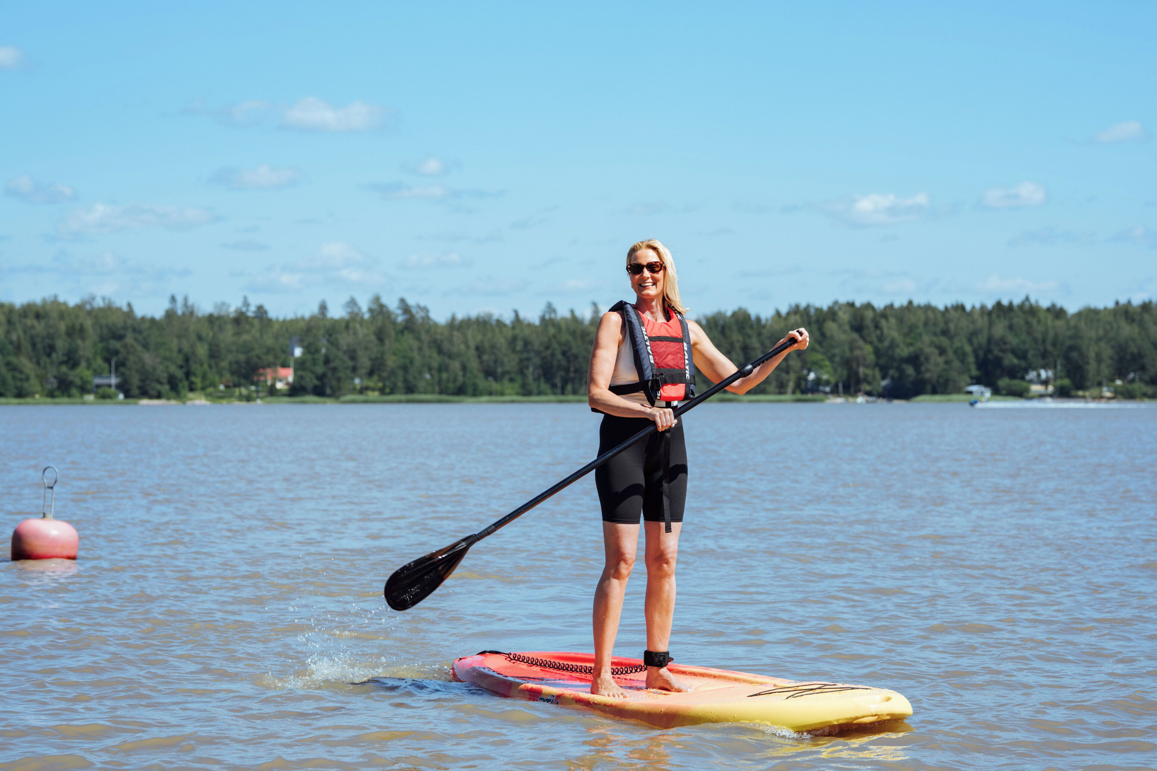 Uma pessoa praticando paddleboard em um lago calmo, com uma margem arborizada ao fundo.