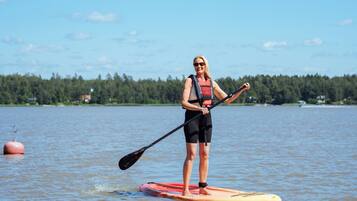 Uma pessoa praticando paddleboard em um lago calmo, com uma margem arborizada ao fundo.