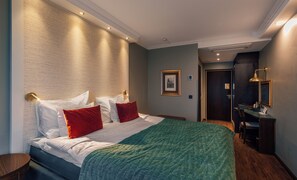 Quarto de hotel com uma cama grande, uma escrivaninha e uma cadeira.