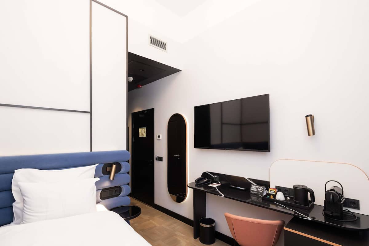 Quarto de hotel moderno com cama, escrivaninha, televisão e pequena cozinha.