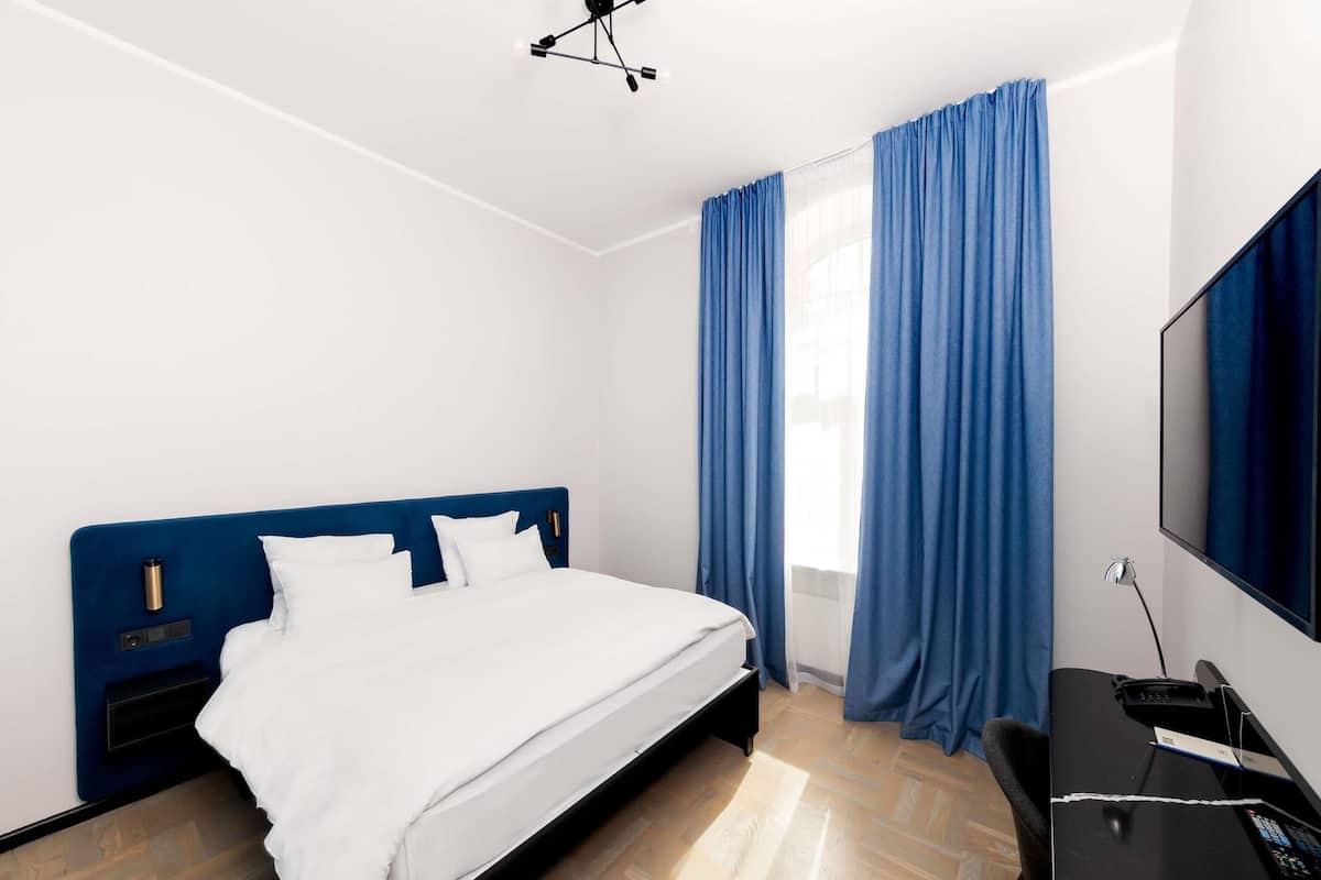 Quarto de hotel moderno com cama, escrivaninha, TV de tela plana e luminária no teto.