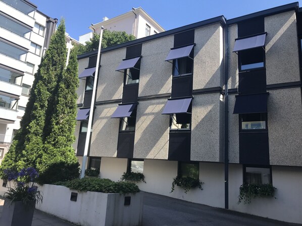 Um edifício moderno com várias janelas e varandas, cercado por vegetação e uma árvore alta.