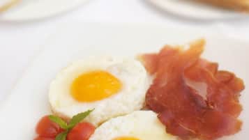 Prato de café da manhã com dois ovos fritos, uma fatia de salmão defumado e tomates cereja em um prato branco.