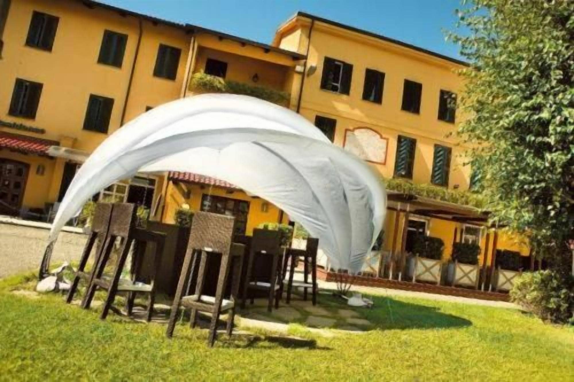 Uma área de estar ao ar livre com toldo branco, cercada por um edifício com várias janelas e fachada amarela.
