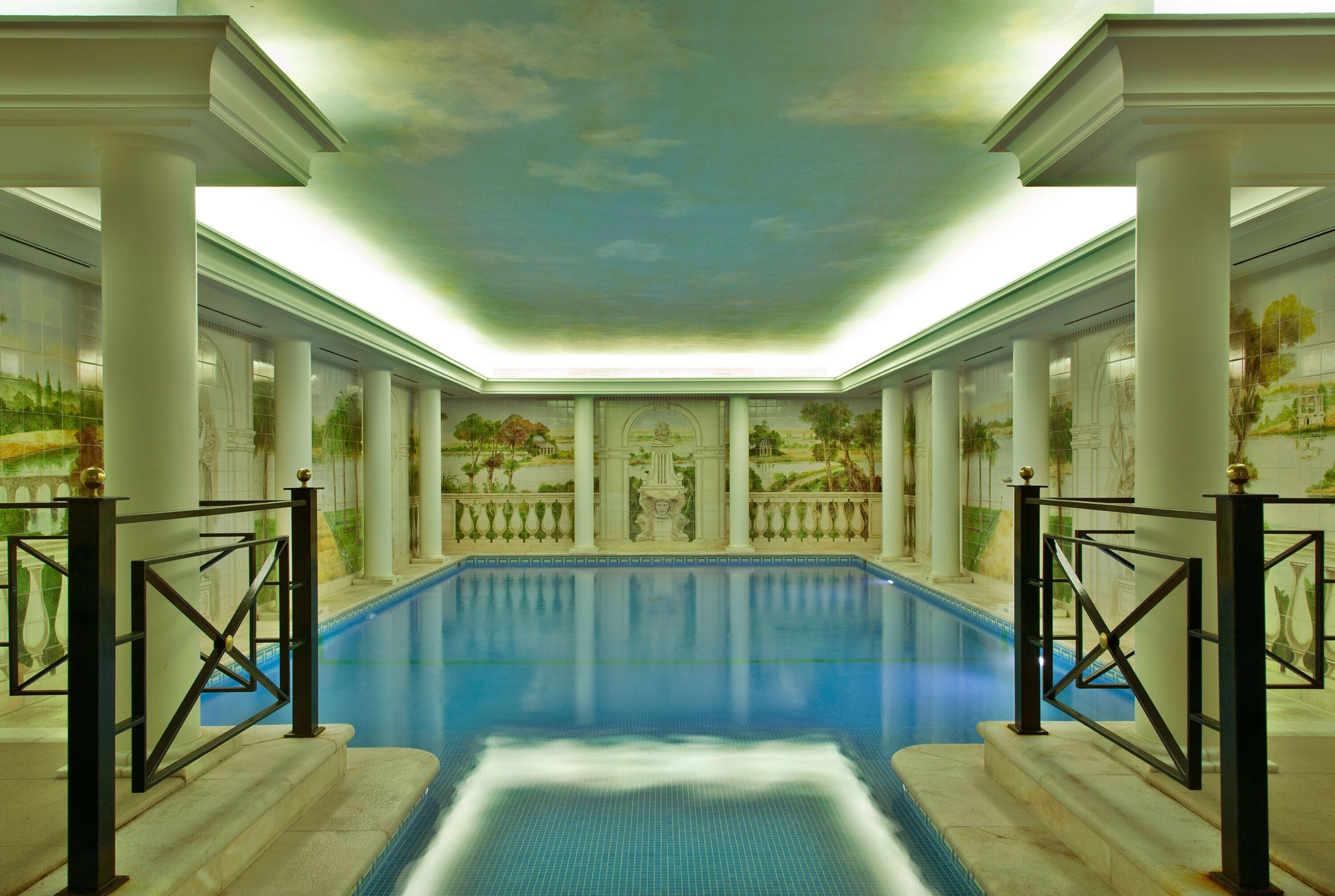 Piscina com um mural nas paredes, cercada por colunas e grades.