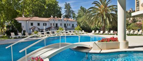 Uma piscina com uma ponte, cadeiras de sol e um edifício ao fundo.
