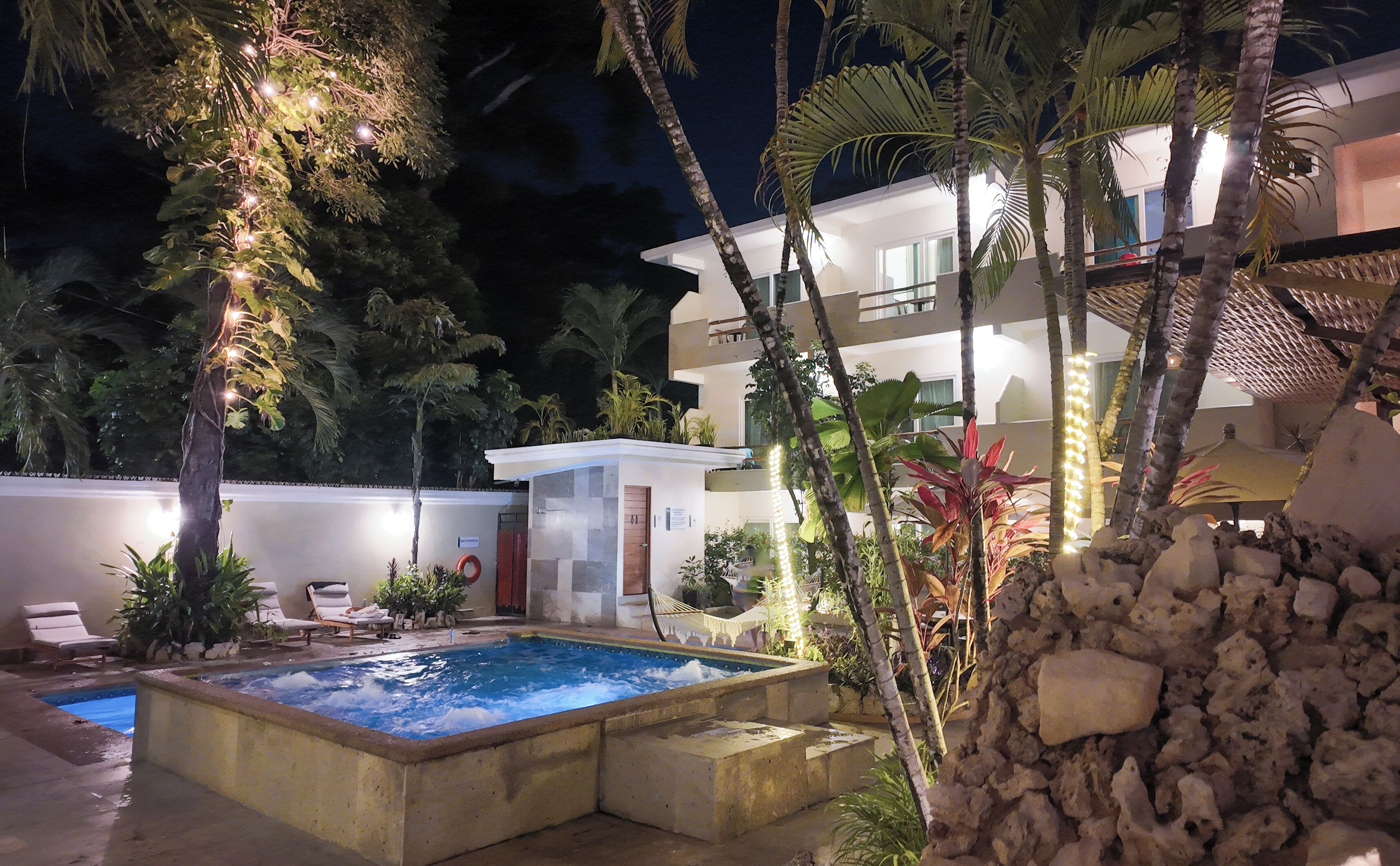 Uma área de piscina com hidromassagem, espreguiçadeiras e um edifício com varandas.
