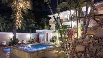 Uma área de piscina com hidromassagem, espreguiçadeiras e um edifício com varandas.