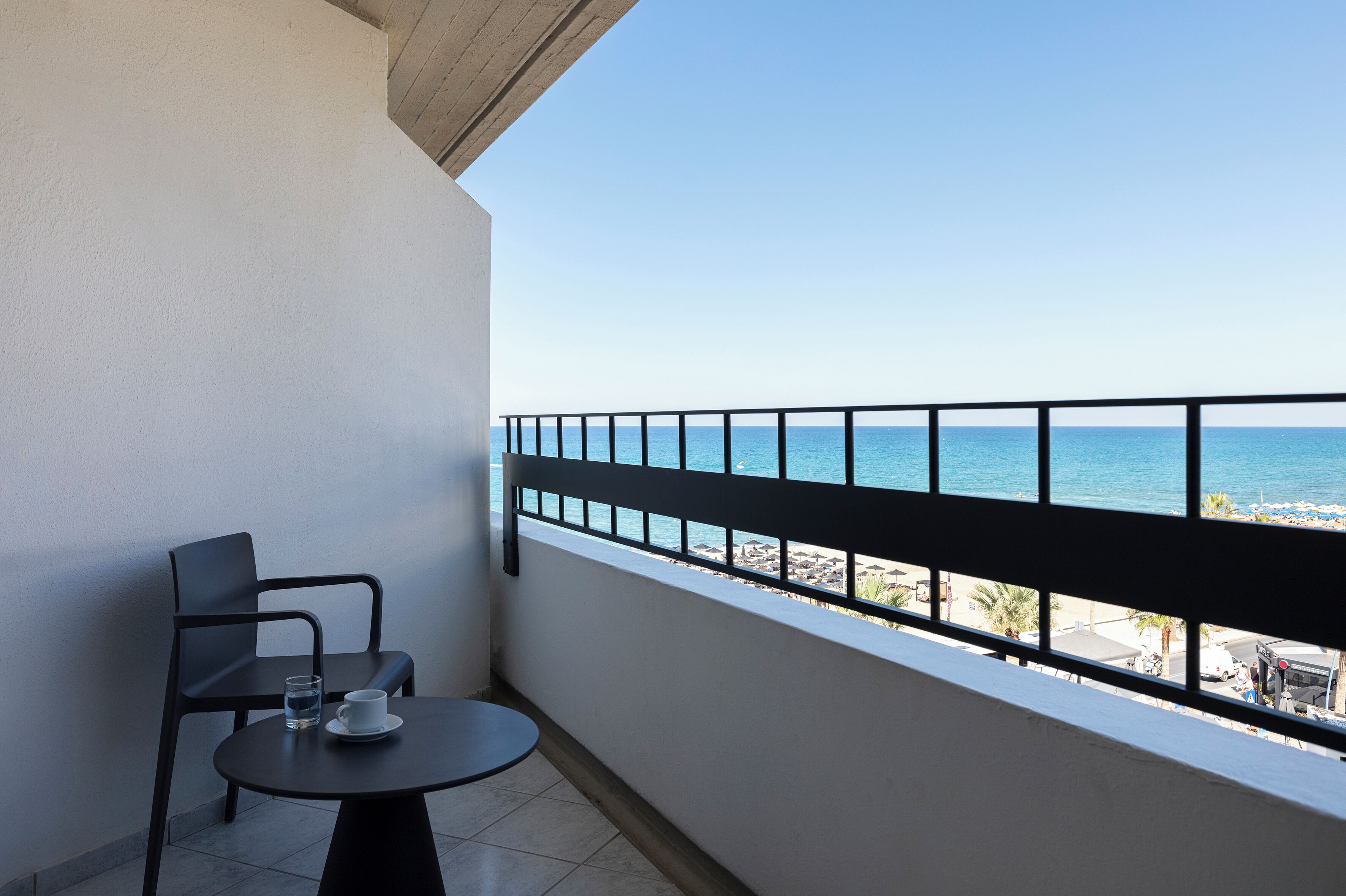 Uma varanda com vista para o mar, uma cadeira, uma mesa e um copo de água.