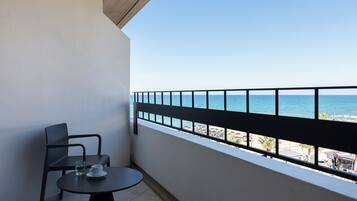 Uma varanda com vista para o mar, uma cadeira, uma mesa e um copo de água.