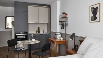 Quarto de hotel pequeno com cozinha compacta, área de refeições, cama e mesa de cabeceira com luminária.