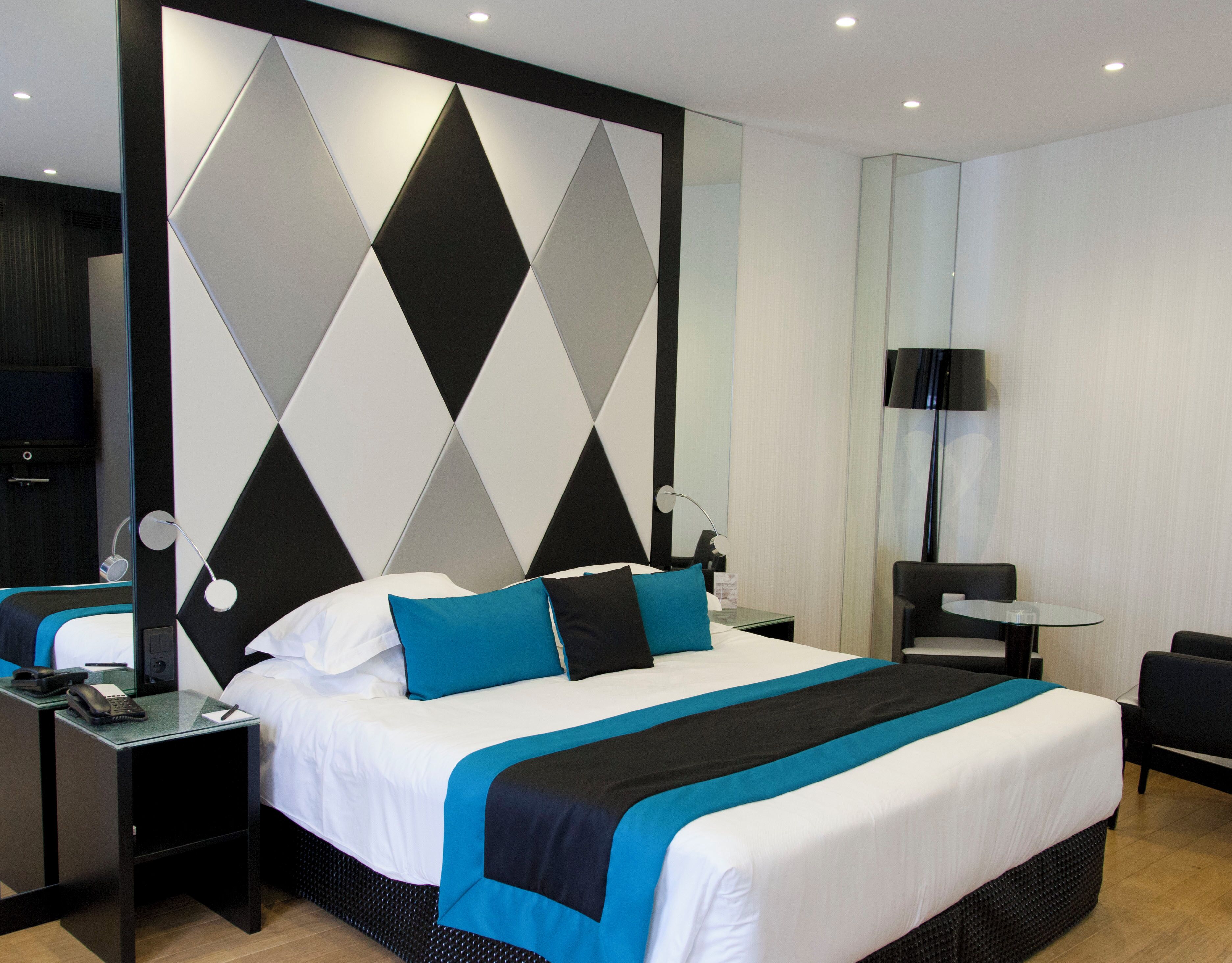 Quarto de hotel moderno com uma cama grande, mesa de cabeceira, escrivaninha, cadeira e luminária.