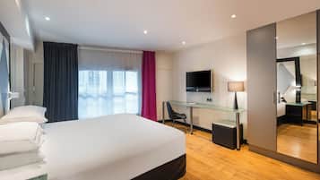 Quarto de hotel moderno com uma cama grande, uma escrivaninha com cadeira, uma televisão de tela plana e um espelho amplo.