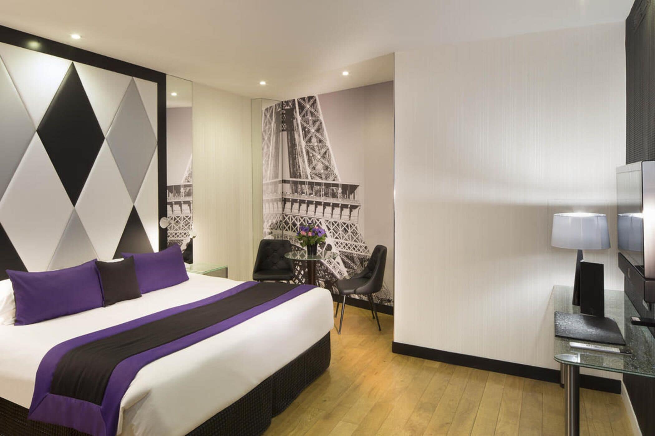 Quarto de hotel com cama, escrivaninha, cadeira e parede com padrão geométrico e imagem de uma ponte.