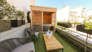 Terraço no topo do prédio com mesa de madeira, duas cadeiras, ofurô e plantas em vasos.