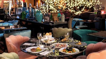 Restaurante com mesas redondas, cadeiras e uma árvore decorativa com luzes.
