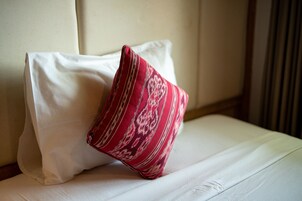 Uma cama com roupa de cama branca e um travesseiro com padrão vermelho.