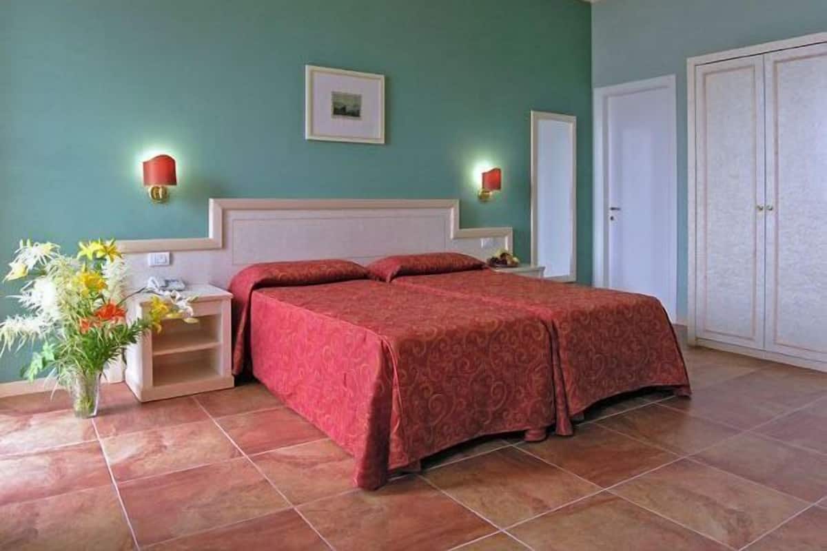 Um quarto com cama, mesas de cabeceira, um vaso de flores e uma porta.