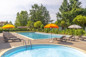 Piscina com espreguiçadeiras e guarda-sóis, cercada por árvores e um céu claro.