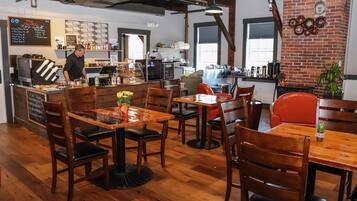 Interior de restaurante com mesas e cadeiras de madeira, área de bar e menu em lousa.