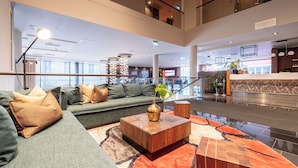 Um hall amplo com um sofá verde, uma mesa de centro de madeira e um lustre moderno.