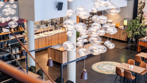 Um hall de hotel moderno com um bar central, áreas de estar e uma escadaria.