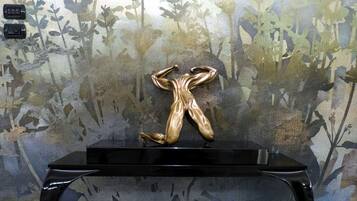 Escultura sobre uma mesa preta, com um mural floral ao fundo.
