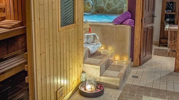 Um espaço de spa rústico com parede de pedra, banheira e um pequeno altar com velas.