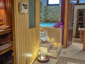 Um espaço de spa rústico com parede de pedra, banheira e um pequeno altar com velas.