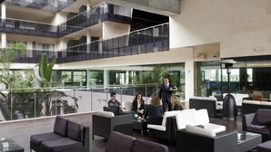 Um lounge interior moderno com várias áreas de estar, paredes de vidro e vista para o exterior.