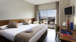 Quarto de hotel com uma cama grande, uma escrivaninha, uma TV e uma varanda com vista.
