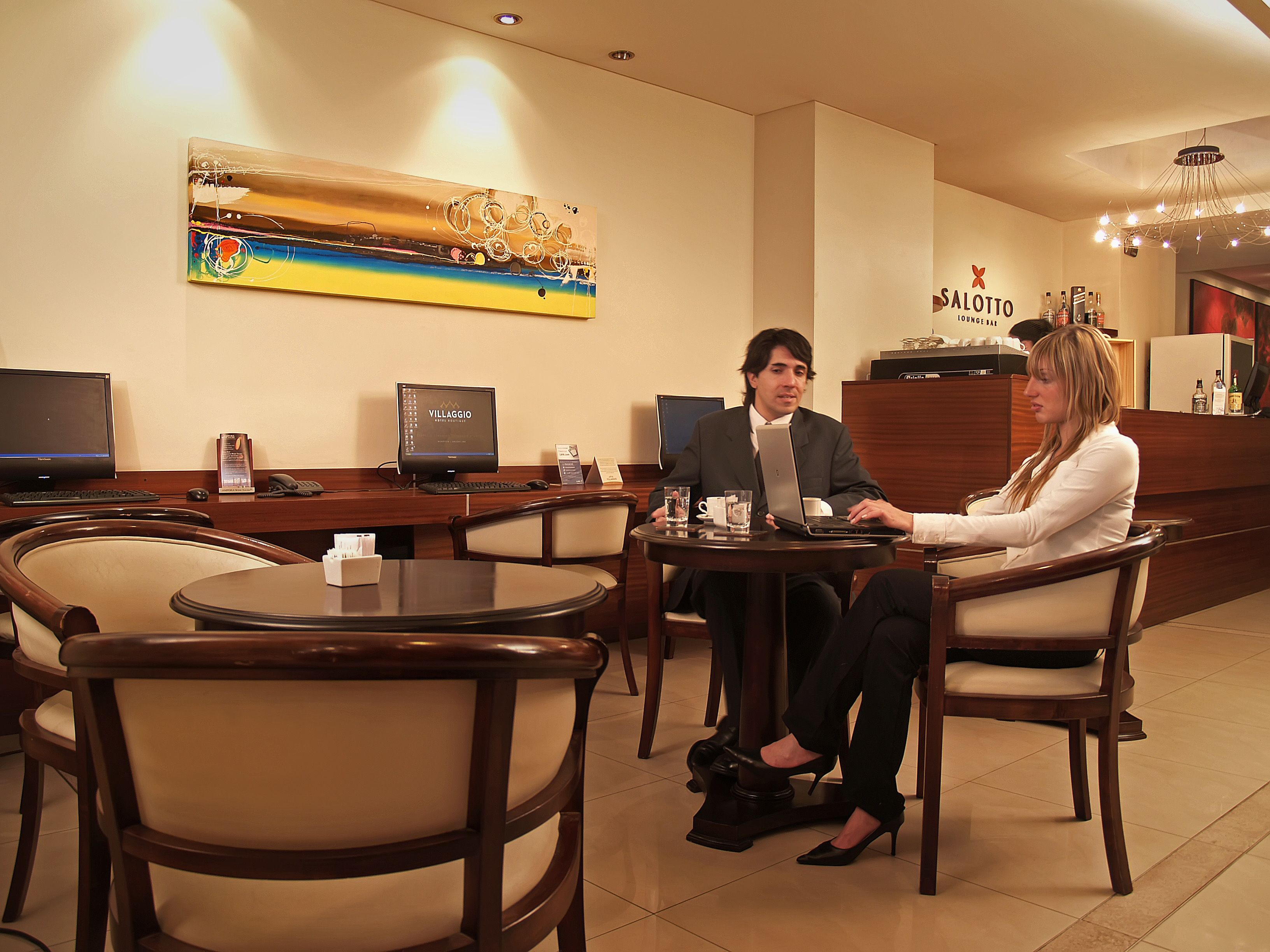Um saguão de hotel com balcão de recepção, uma pintura na parede e área de bar.